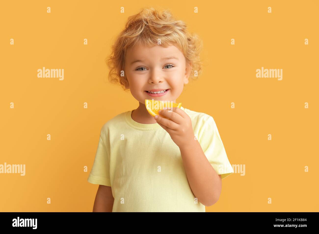 Cute little boy eating orange on color background Stock Photo - Alamy