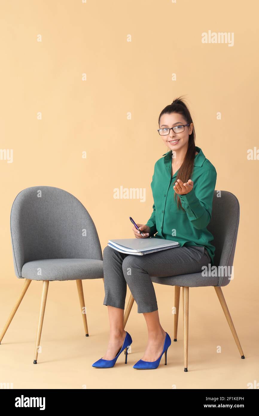 Portrait of female psychologist sitting on chair against color ...