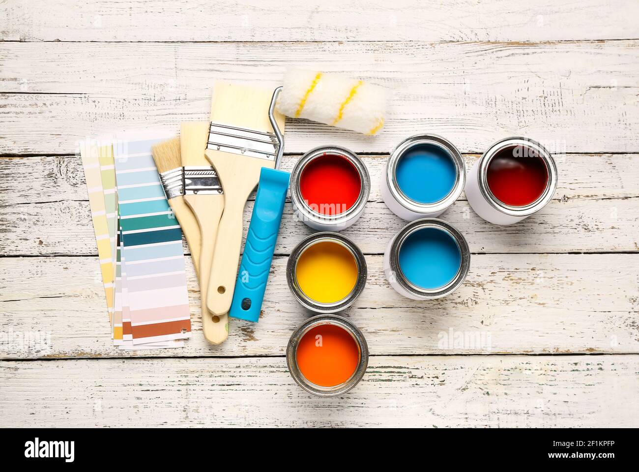 Cans of paints with palette samples, brushes and roller on light wooden ...
