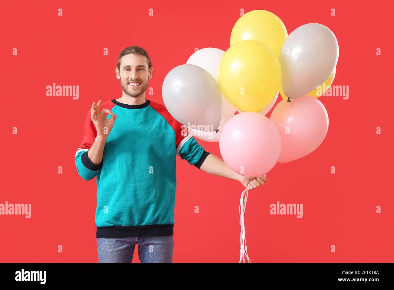 Handsome young man with balloons showing OK on color background Stock ...