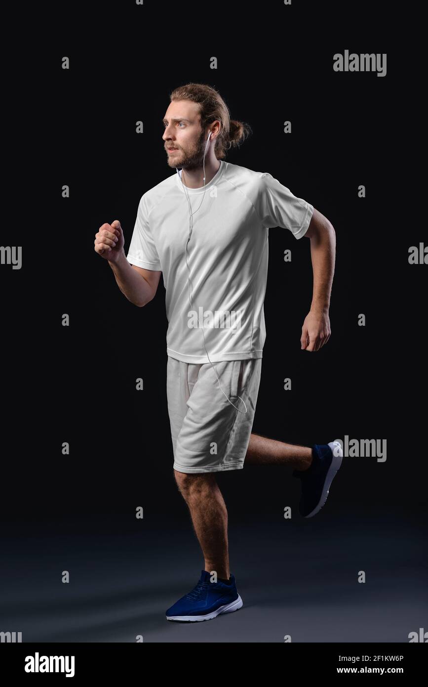 Sporty male runner listening to music on dark background Stock Photo ...