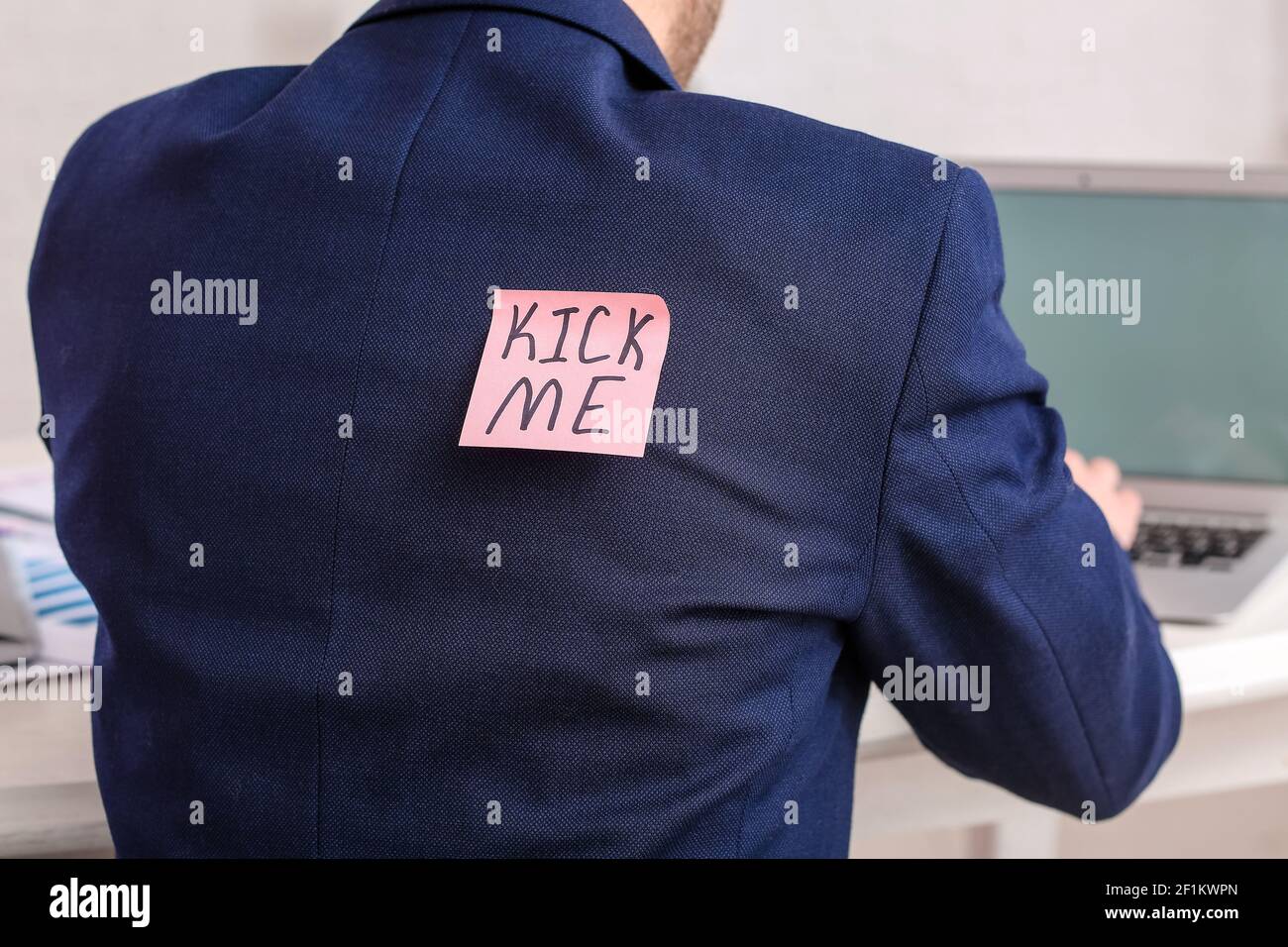Sticky note with text KICK ME on back of man working in office. April ...