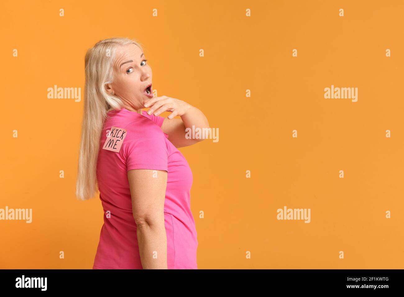 Sticky note with text KICK ME on back of mature woman against color ...