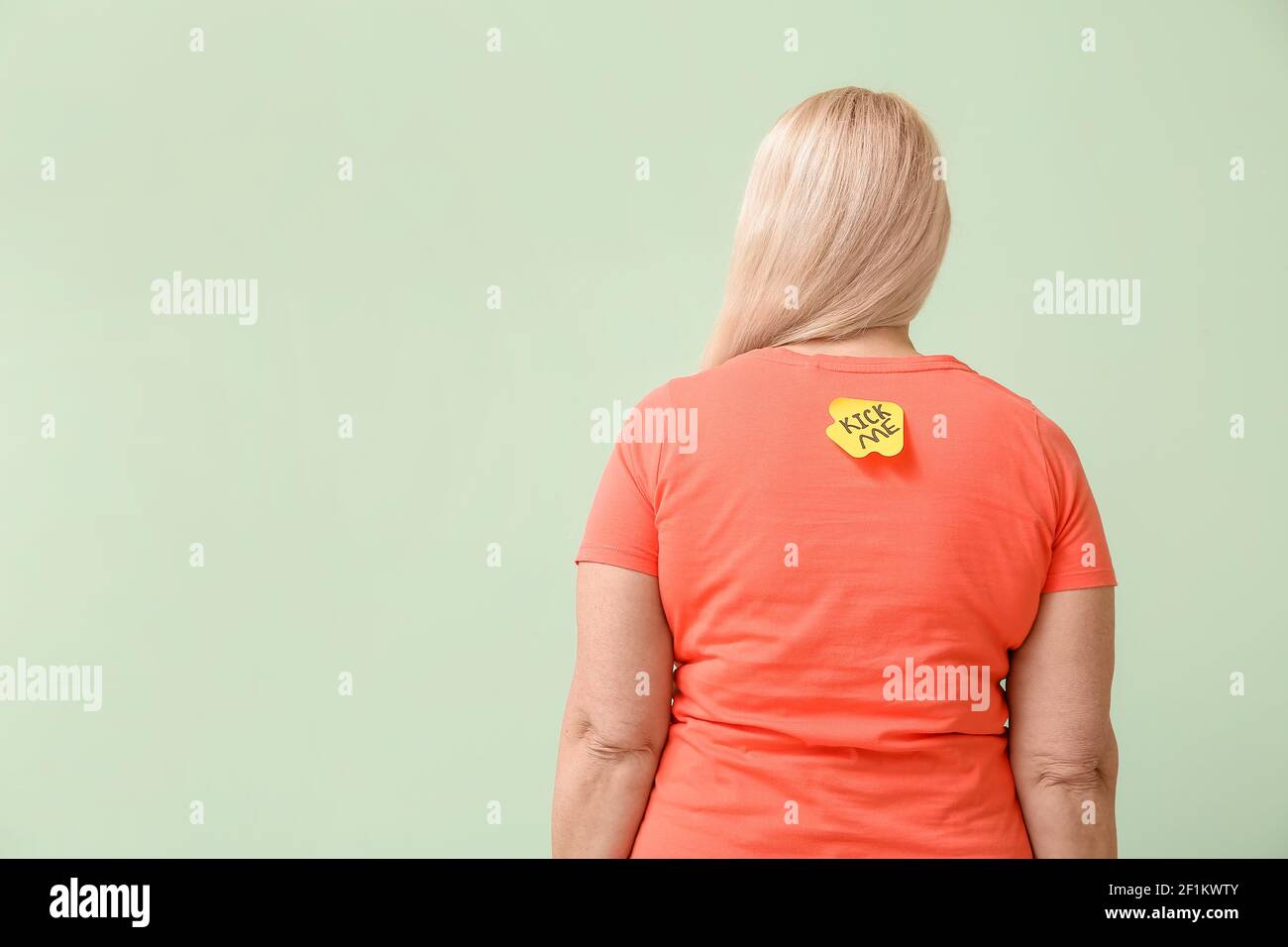 Sticky note with text KICK ME on back of mature woman against color ...