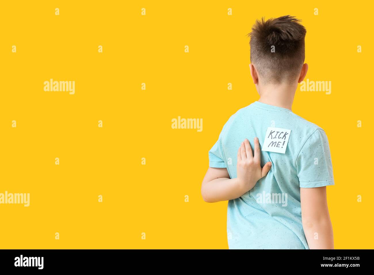 Sticky note with text KICK ME on back of little boy against color ...