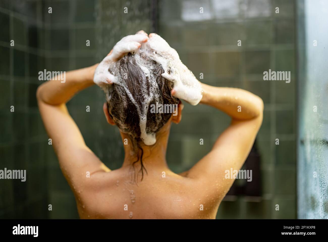 Woman staying back in shower apply shampoo with water dripping. Taking ...