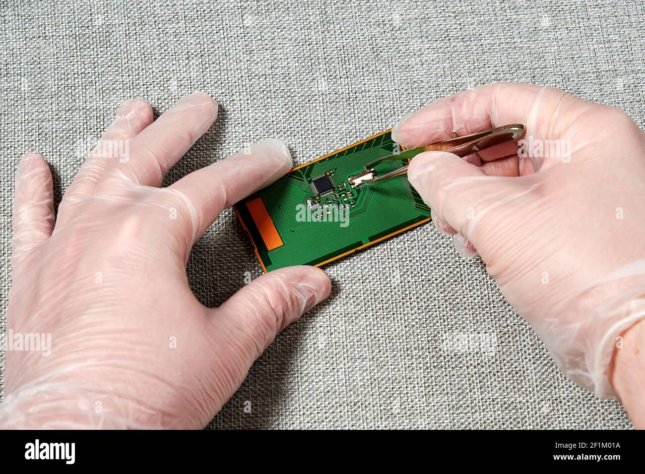 Worker hands with tweezers repairing the pcb with a small microchip ...