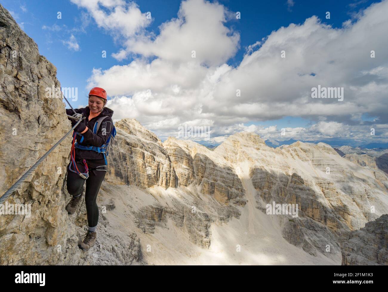Attractive blonde female mountain climber on a steep Via Ferrata in the ...