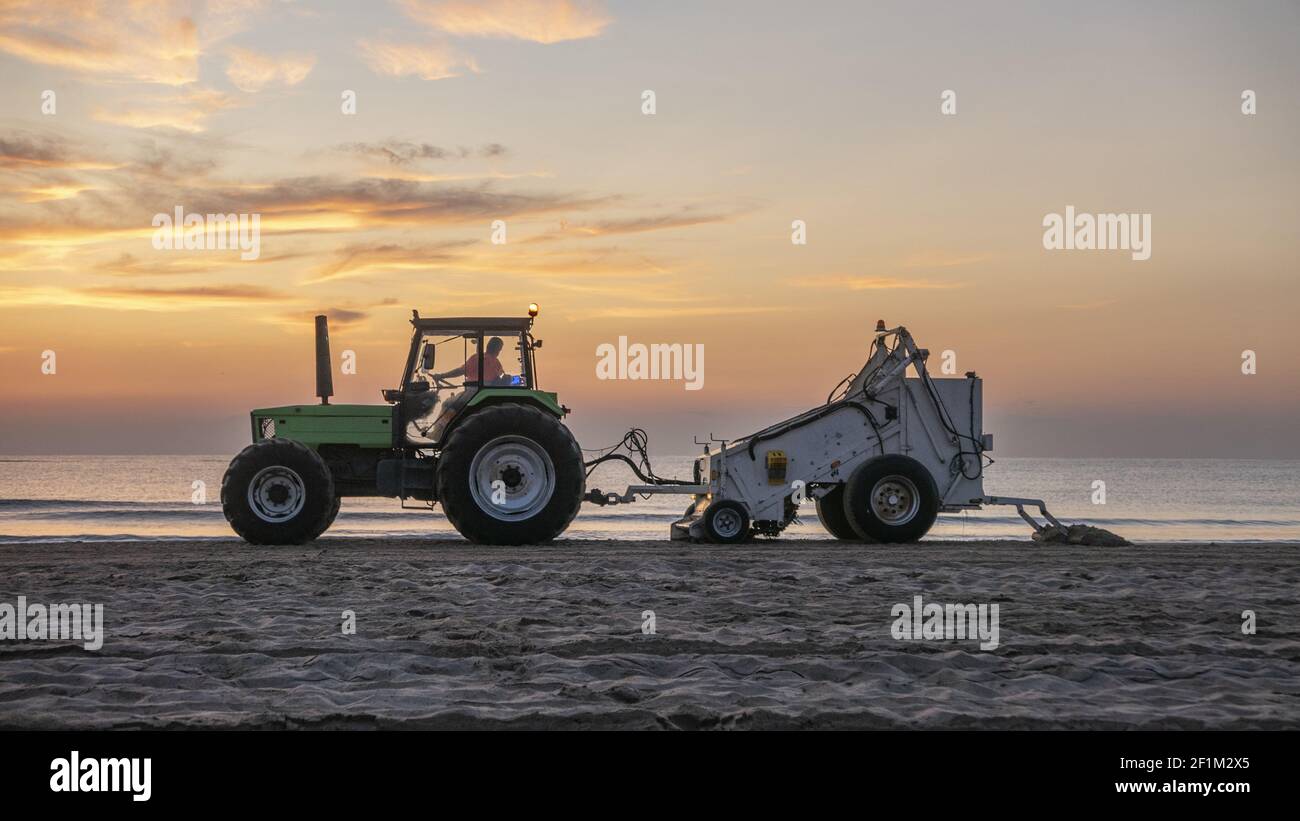 Tractor cleaning the sand on the beach early with sunrise background ...