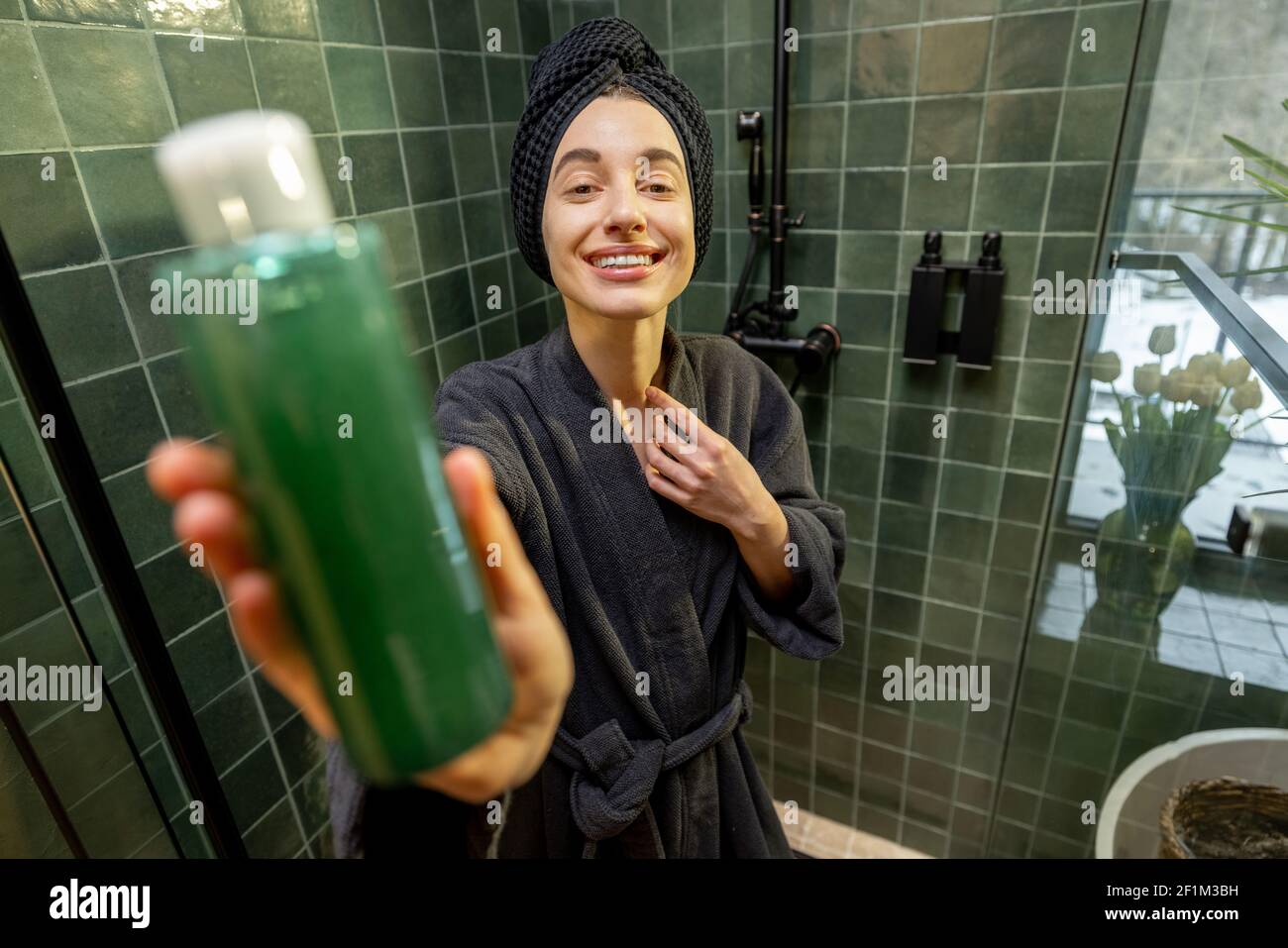 Woman after shower holding and showing at camera a bottle with green ...