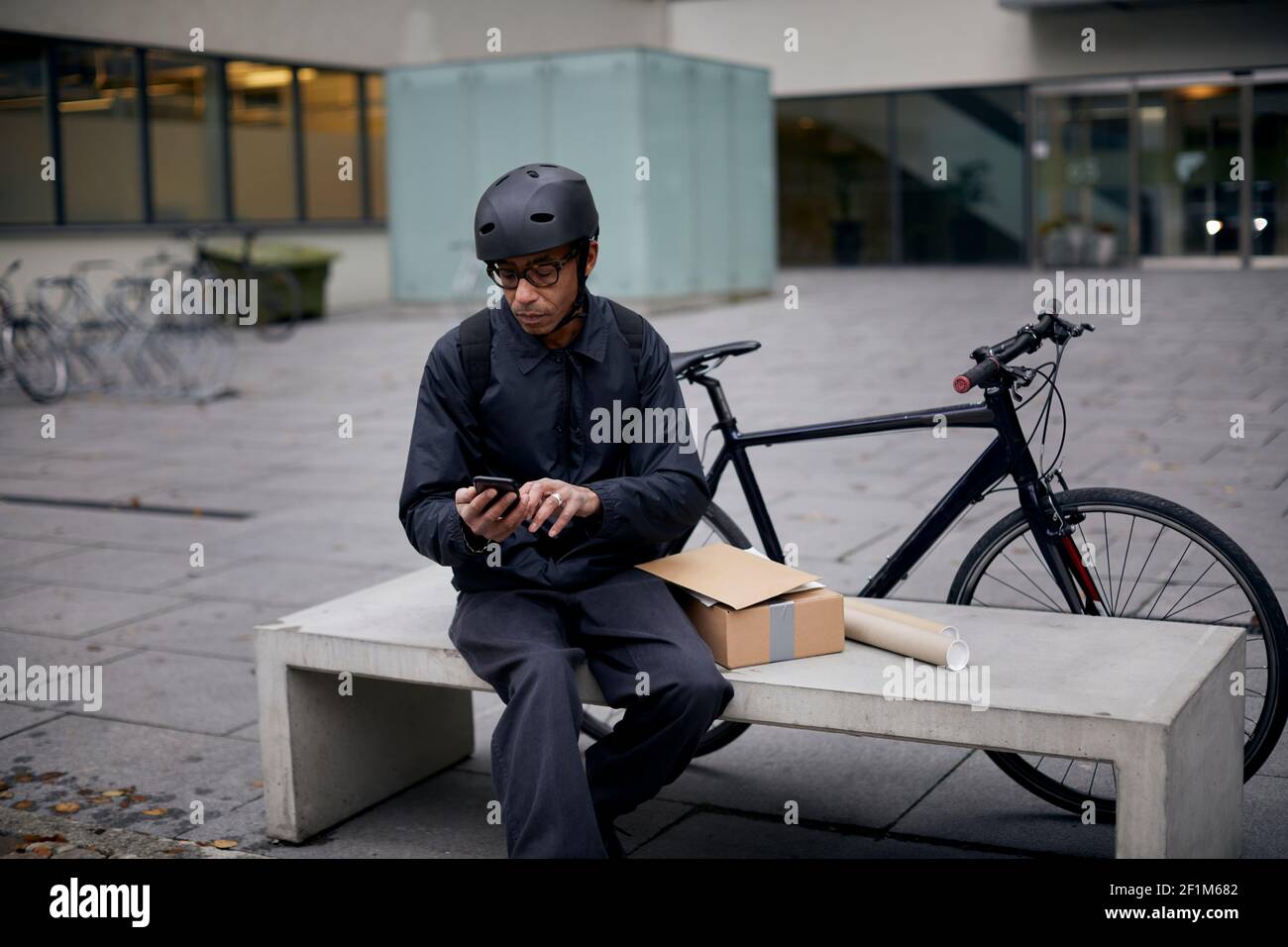 Bicycle courier using cell phone on bench Stock Photo - Alamy