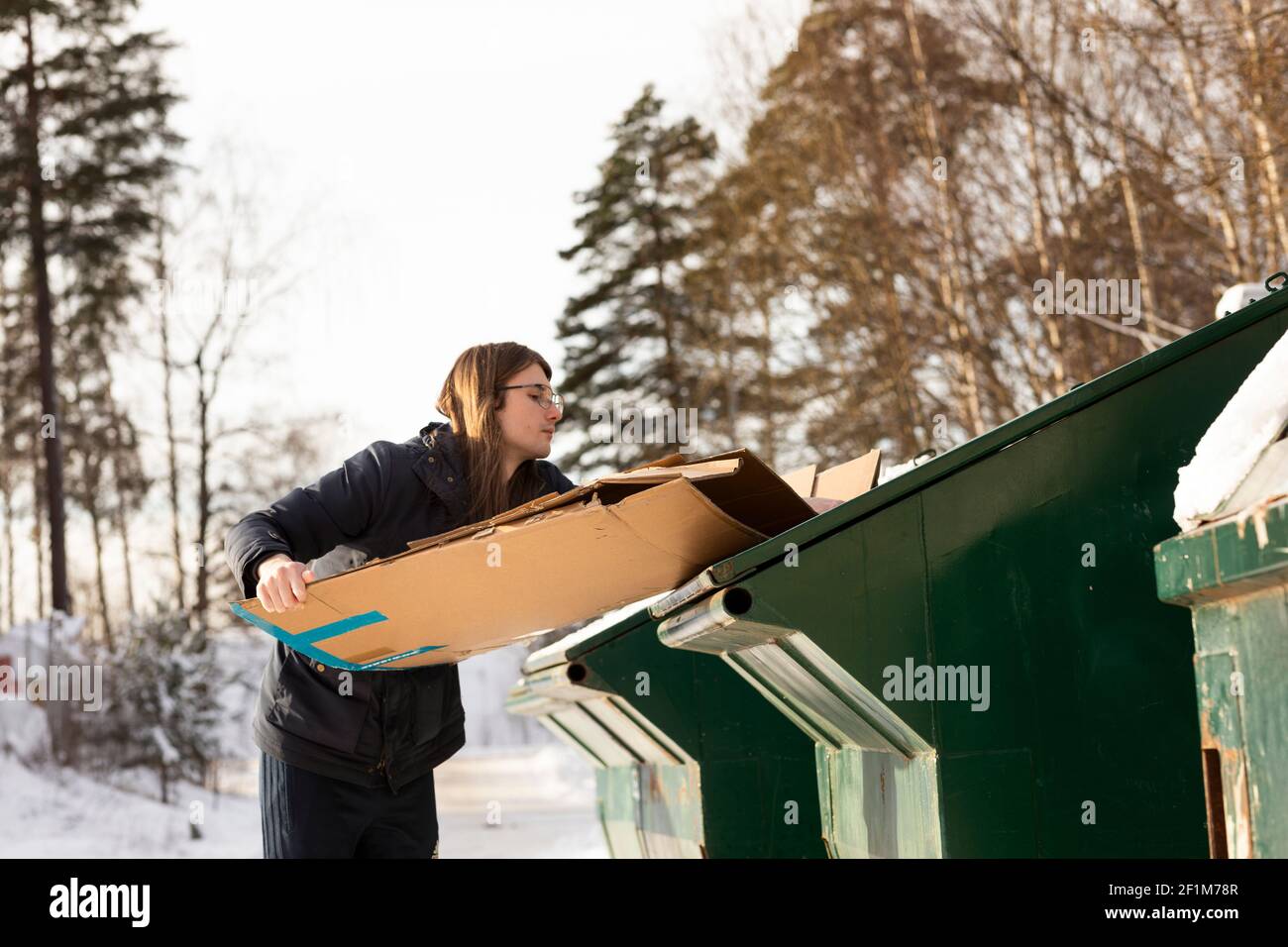 Young man putting cardboard box into recycling bin Stock Photo - Alamy