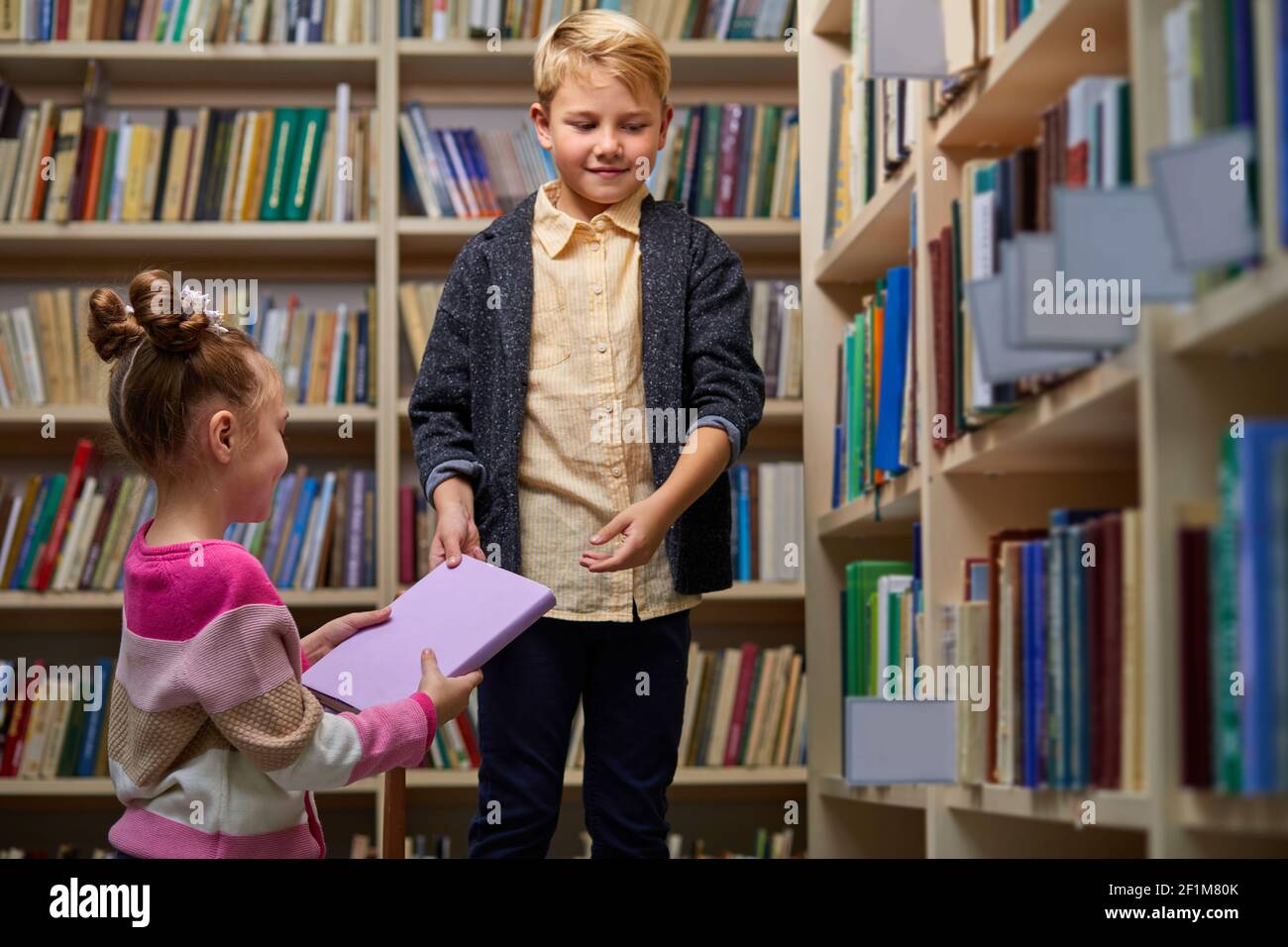 friendly children giving books to each other, help in library before ...