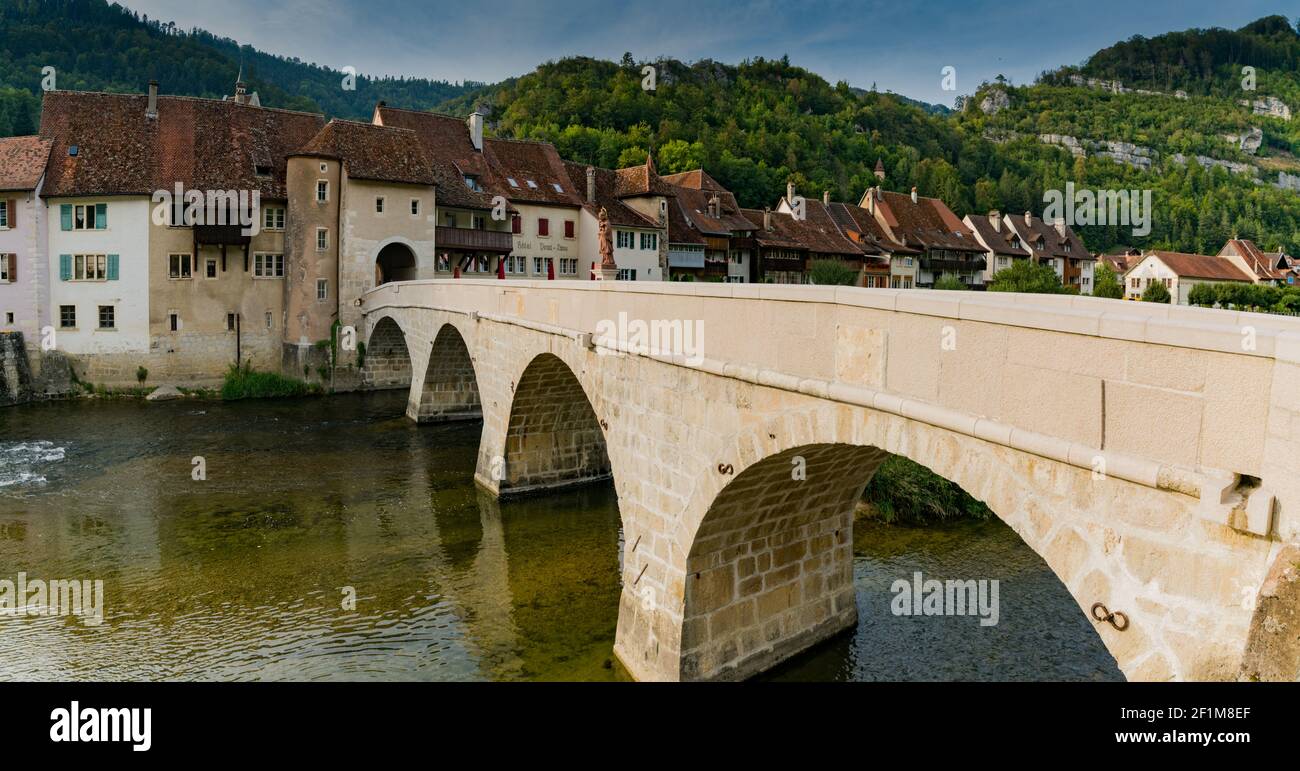 Old stone bridge over a river leads to a picturesque historic European ...