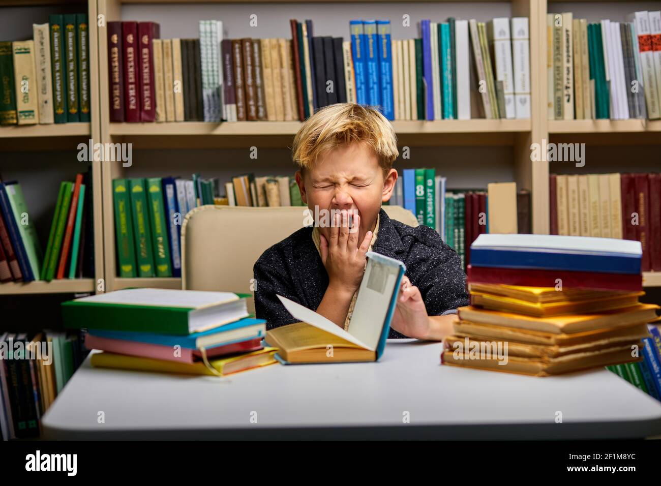 exhausted kid boy yawning while studying, doing homework, sitting at ...