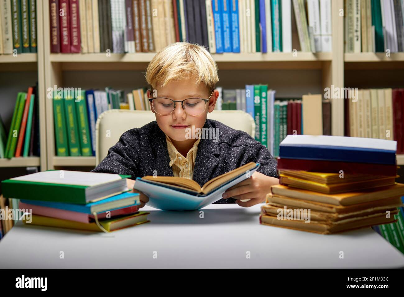 school boy reading book while preparing for lesson in library, diligent ...