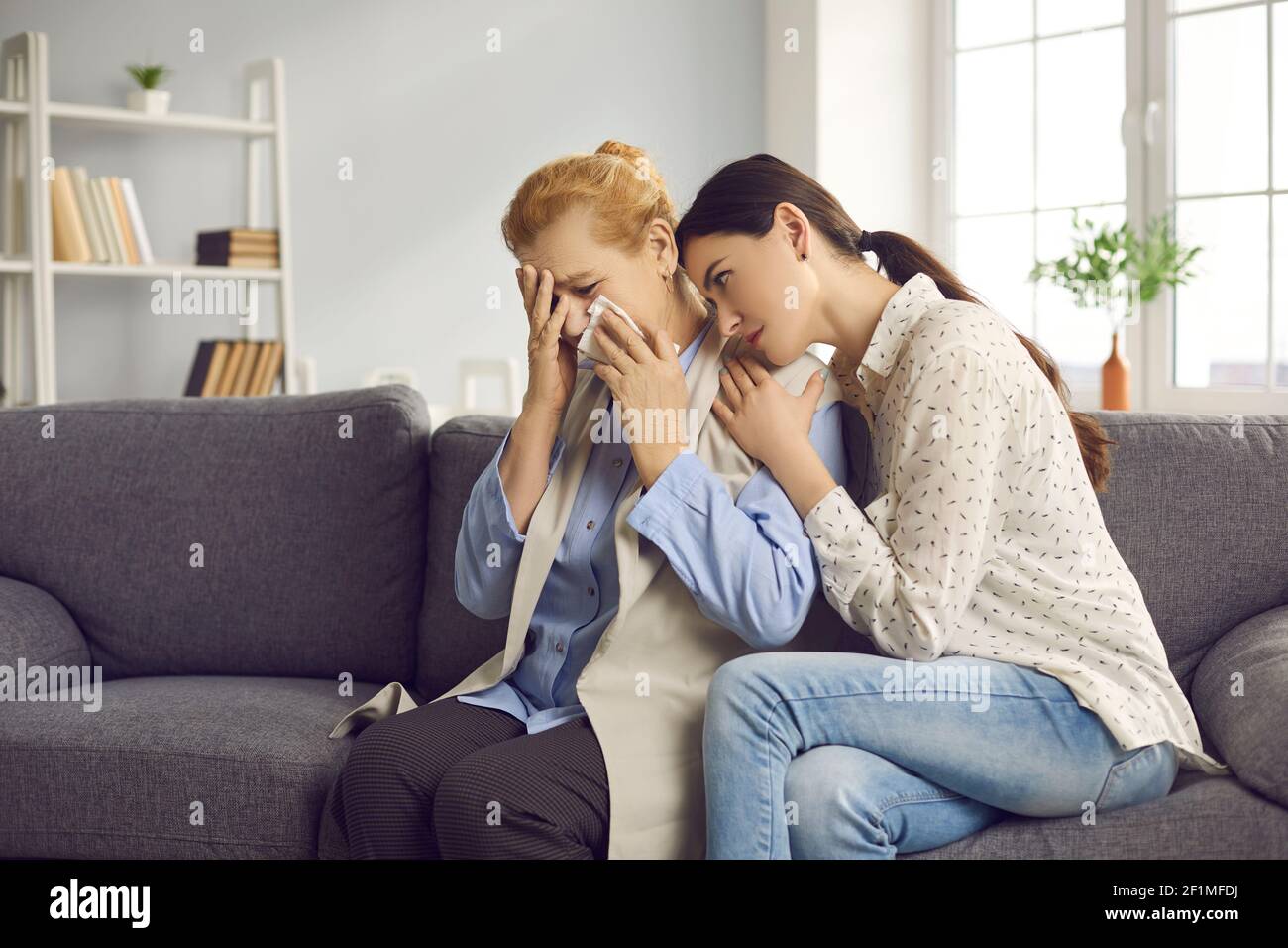 Young daughter comforting her senior mother who's crying sitting on ...