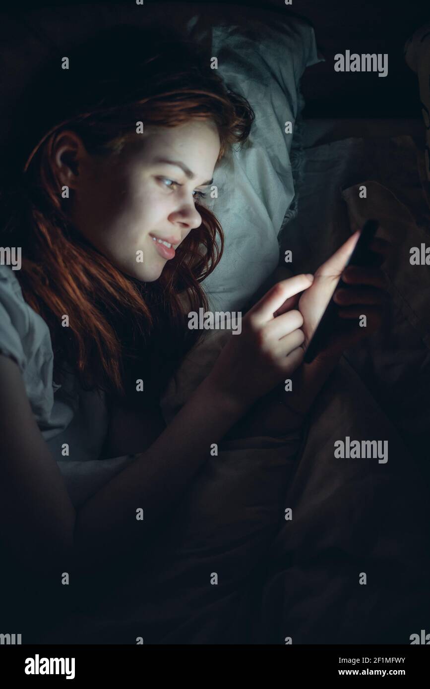 emotional woman with phone in hands at night lying in bed technology ...