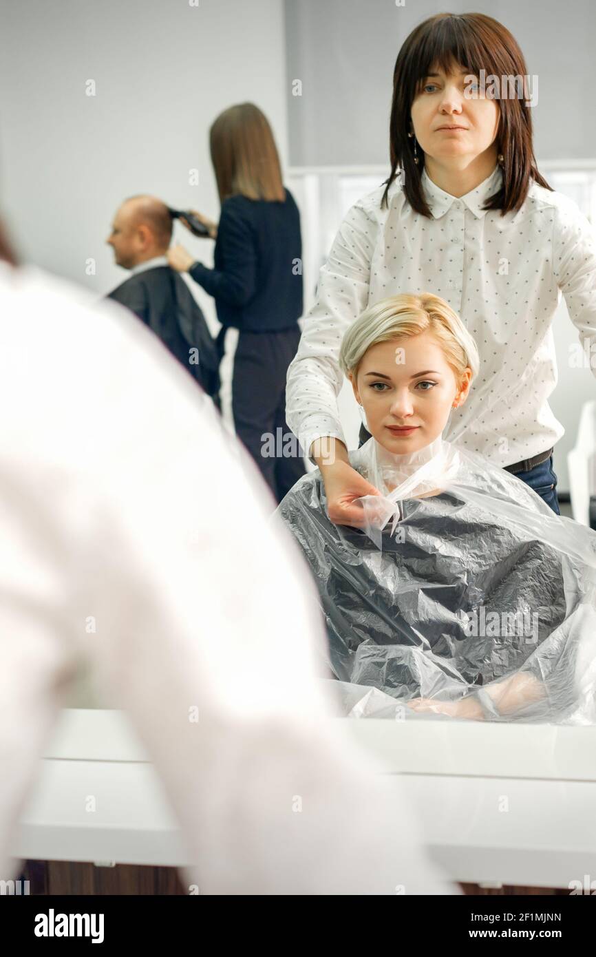 The female hairdresser puts on a transparent cellophane cape to the ...