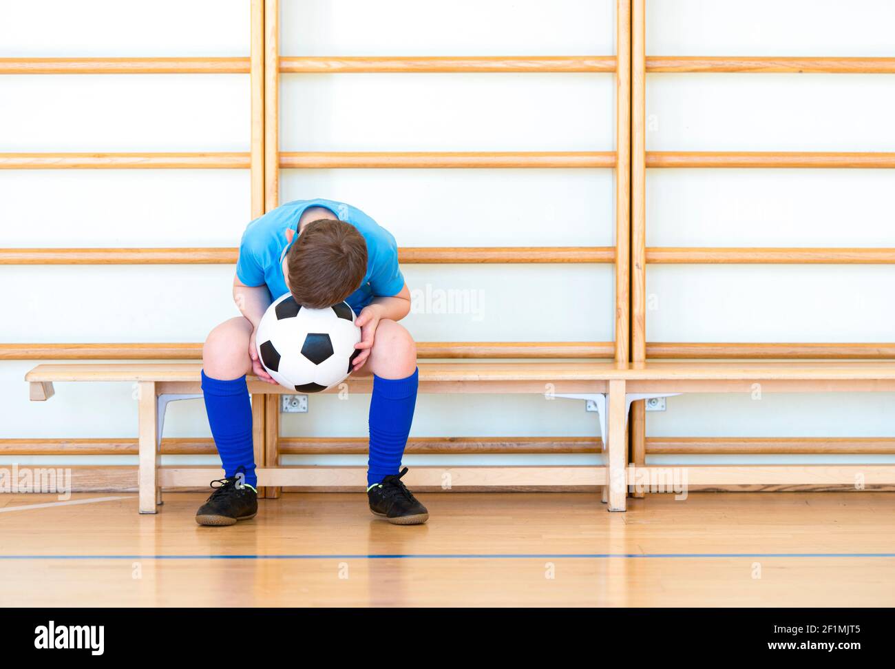 Sad disappointed boy with soccer ball in a physical education lesson ...
