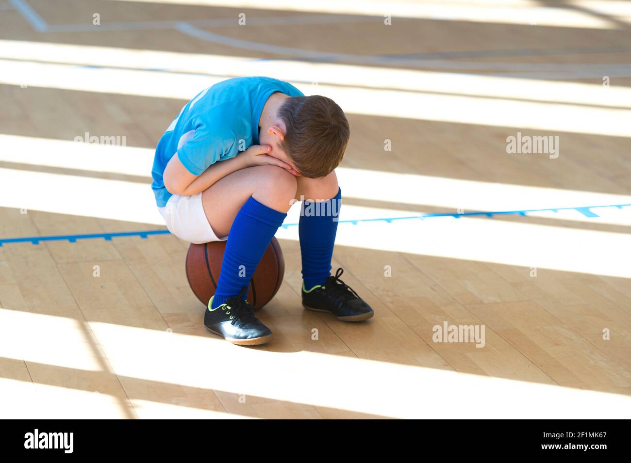Sad disappointed boy sitting on basketball ball in a physical education ...