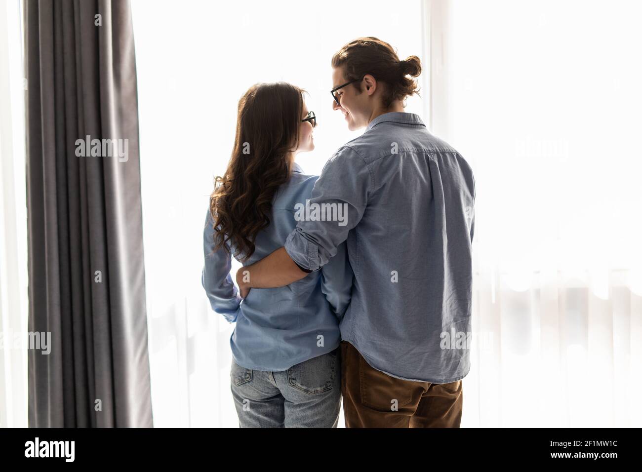Back view of beautiful young couple looking out the window and hugging ...