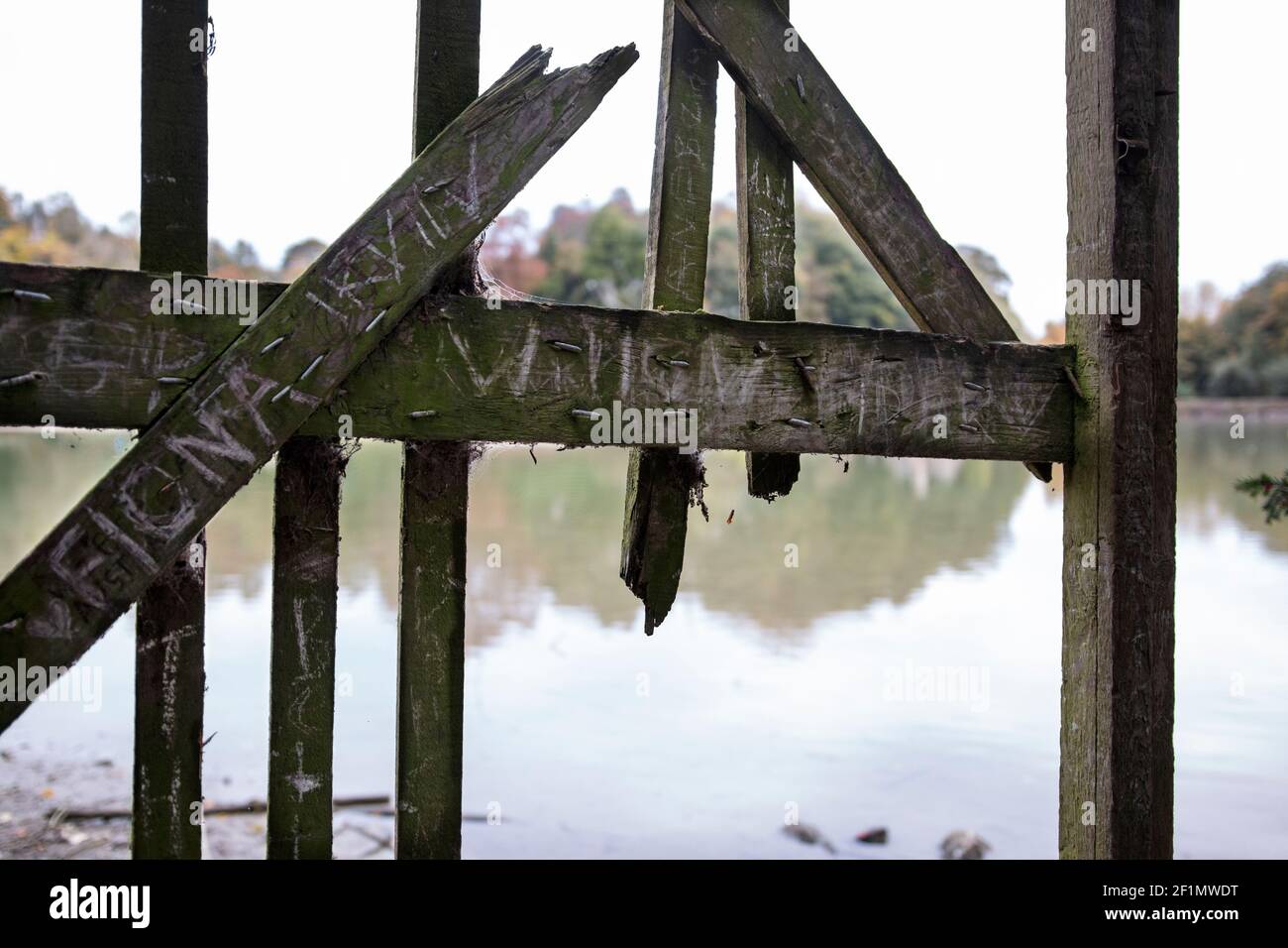 graffiti written on wooden posts on an old building next to a lake in ...