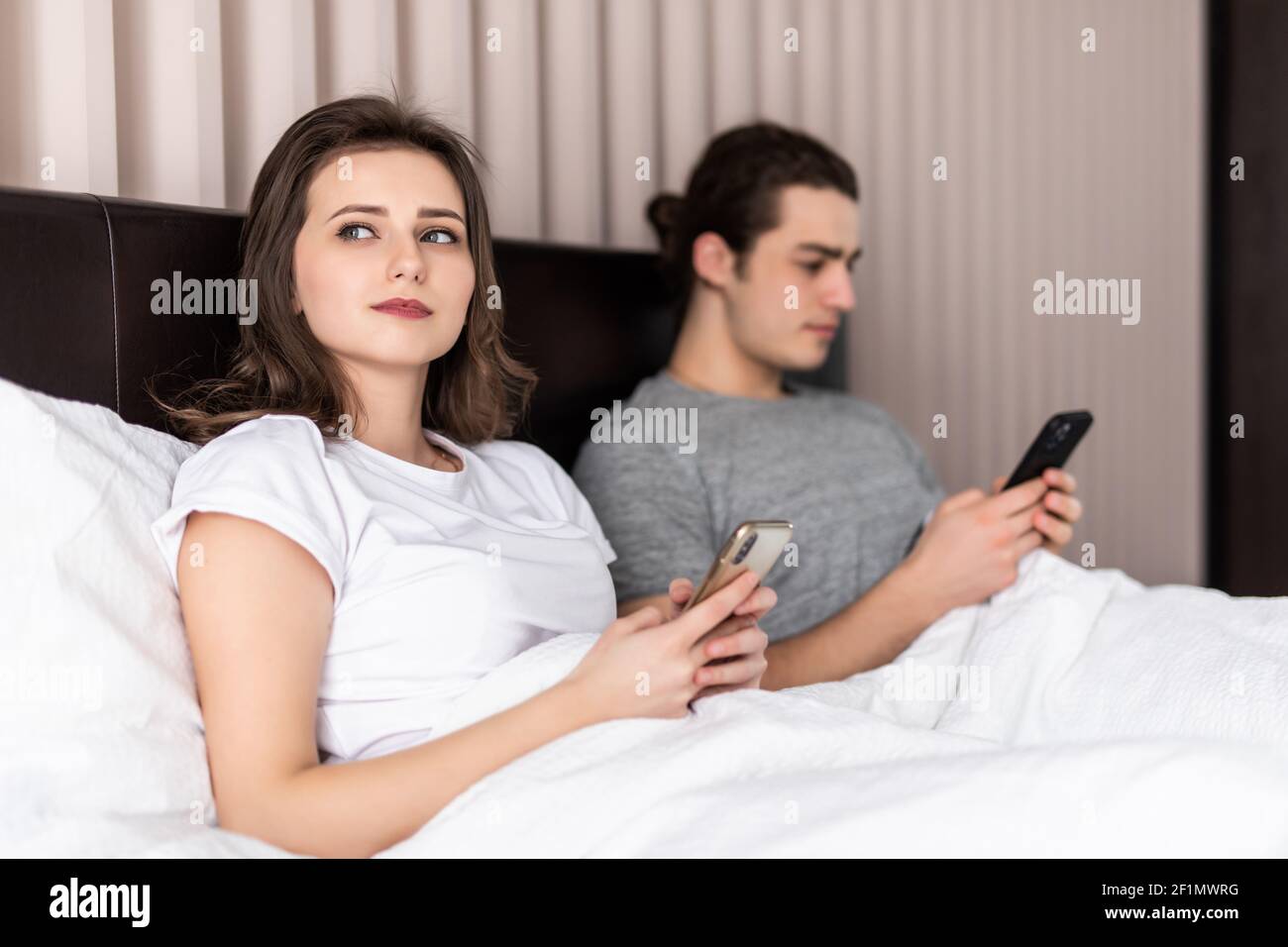 Happy couple chatting on mobile after waking up lying in bed. Man ...