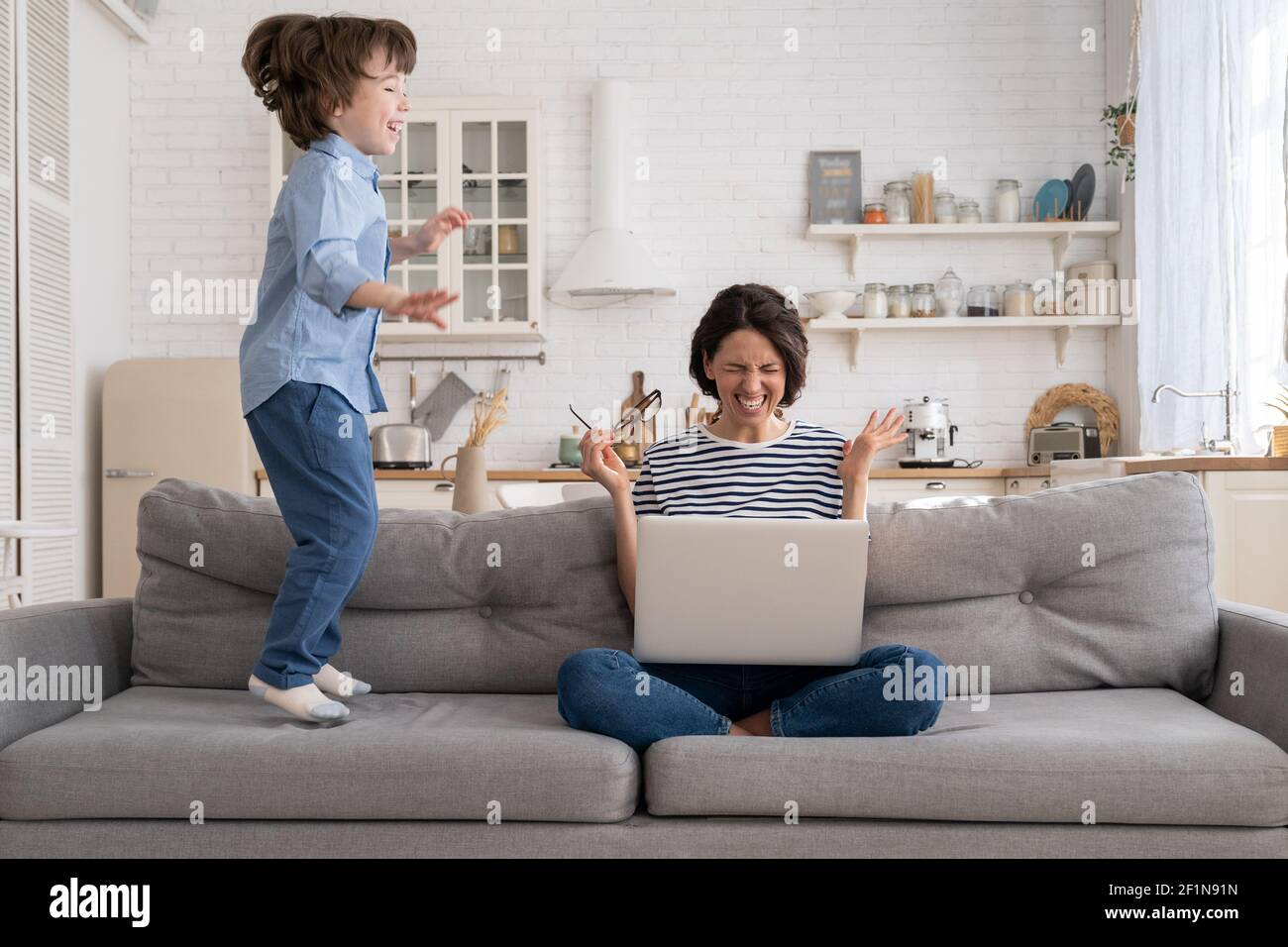 Tired mother sit on couch, work on laptop at home, hyperactive little ...