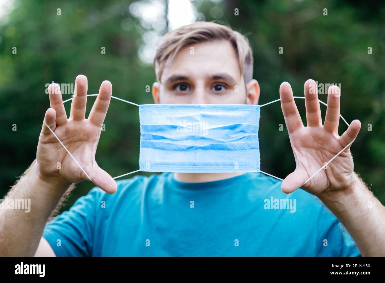 Scared Caucasian man holding blue medical mask in front of his face ...