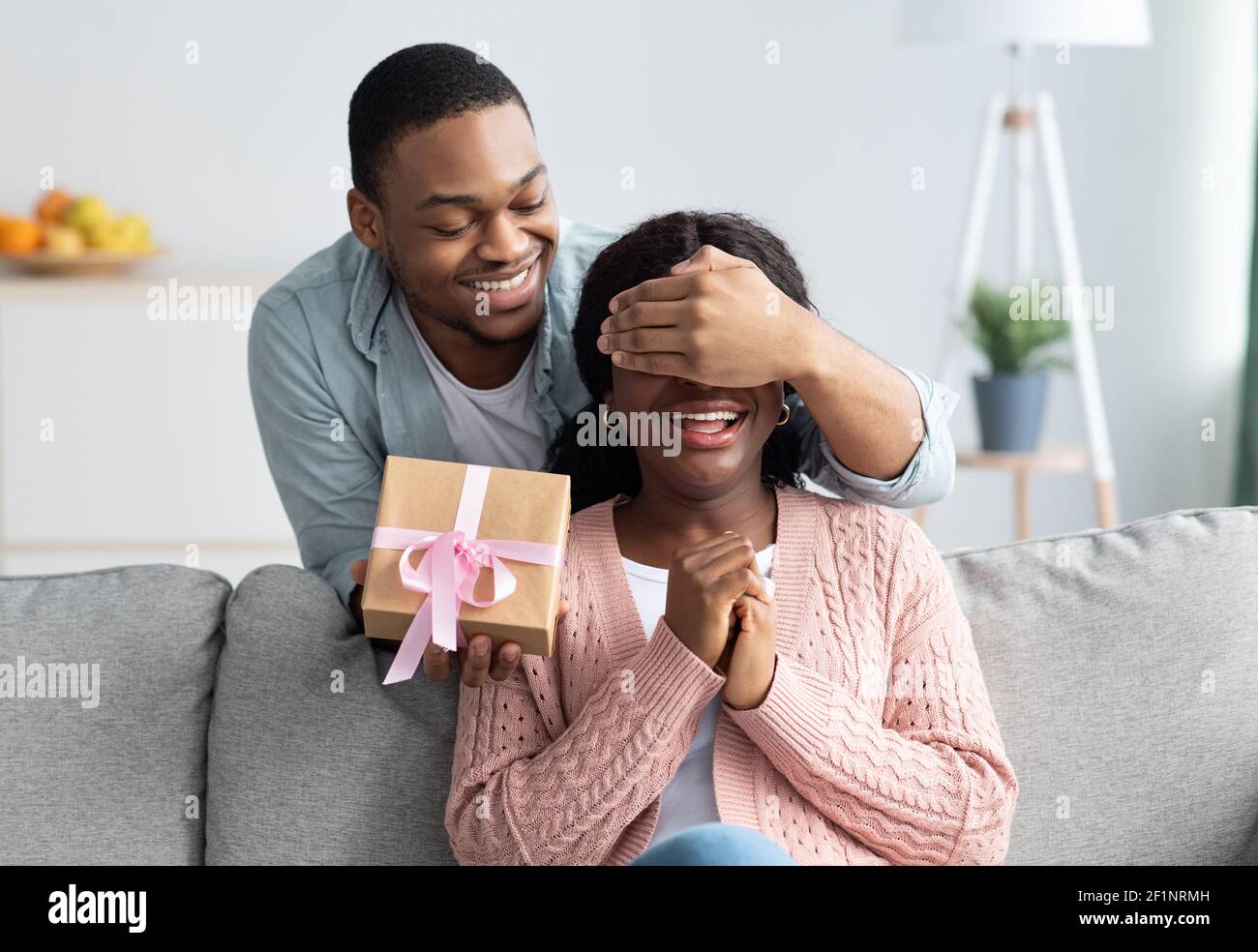 Cheerful black man making surprise for his excited wife at home. Happy ...