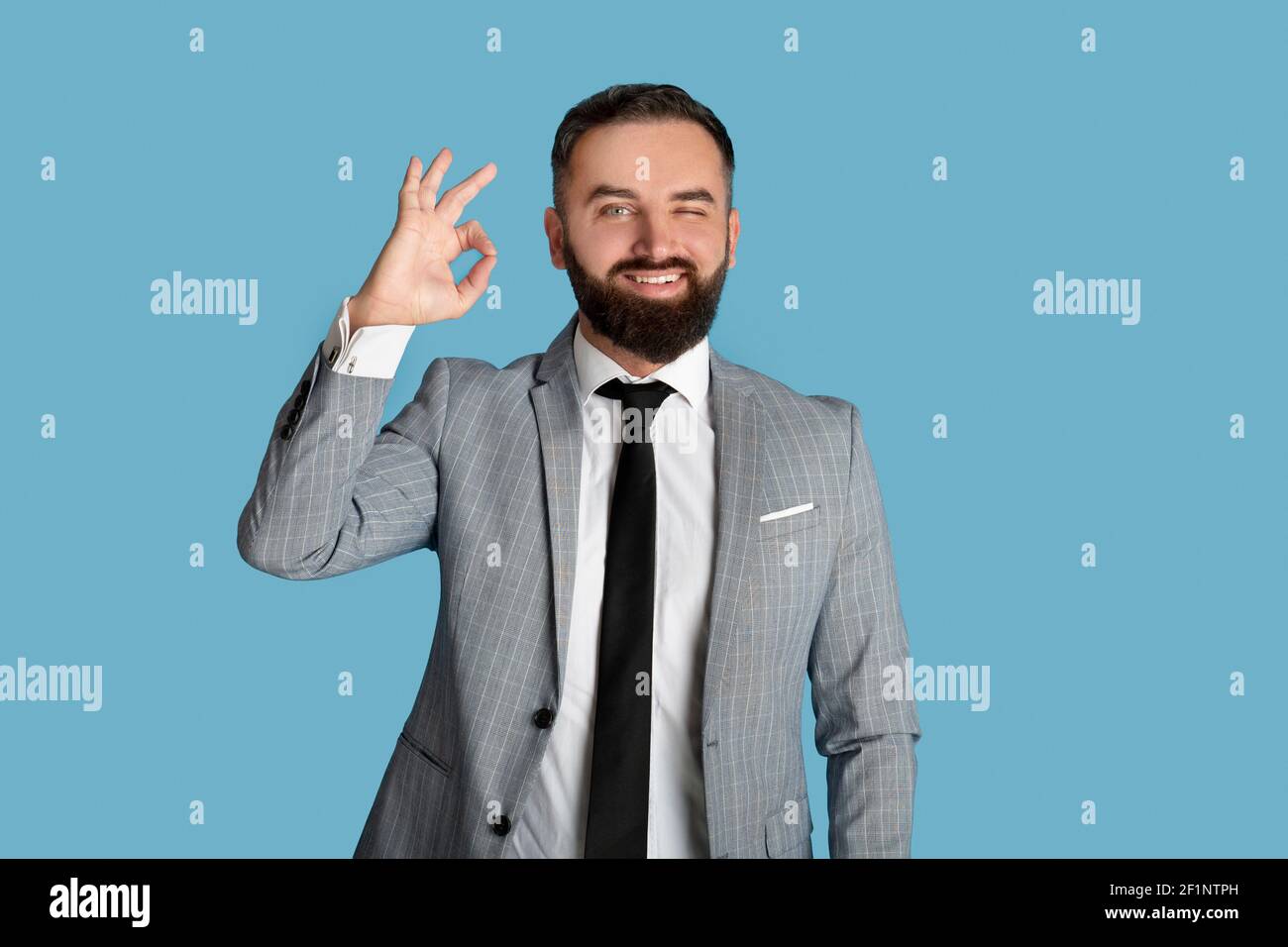 Cheerful young businessman in formalwear showing okay gesture on blue ...