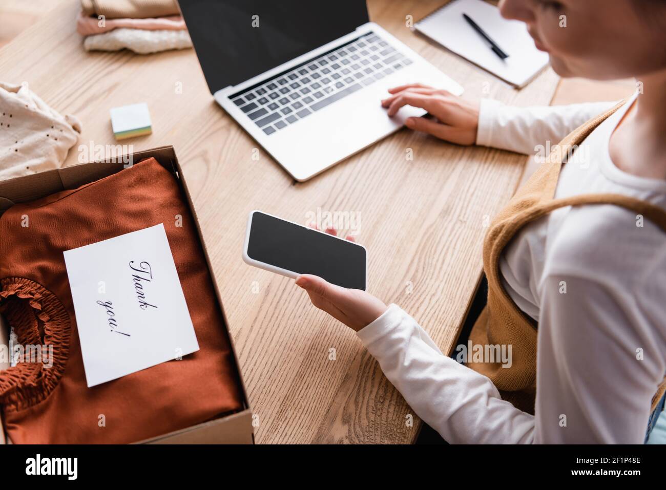 partial view of showroom owner holding smartphone with blank screen at ...