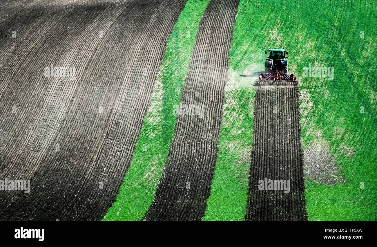 Sunshine view of big tractor plowing the ground of green field on the ...