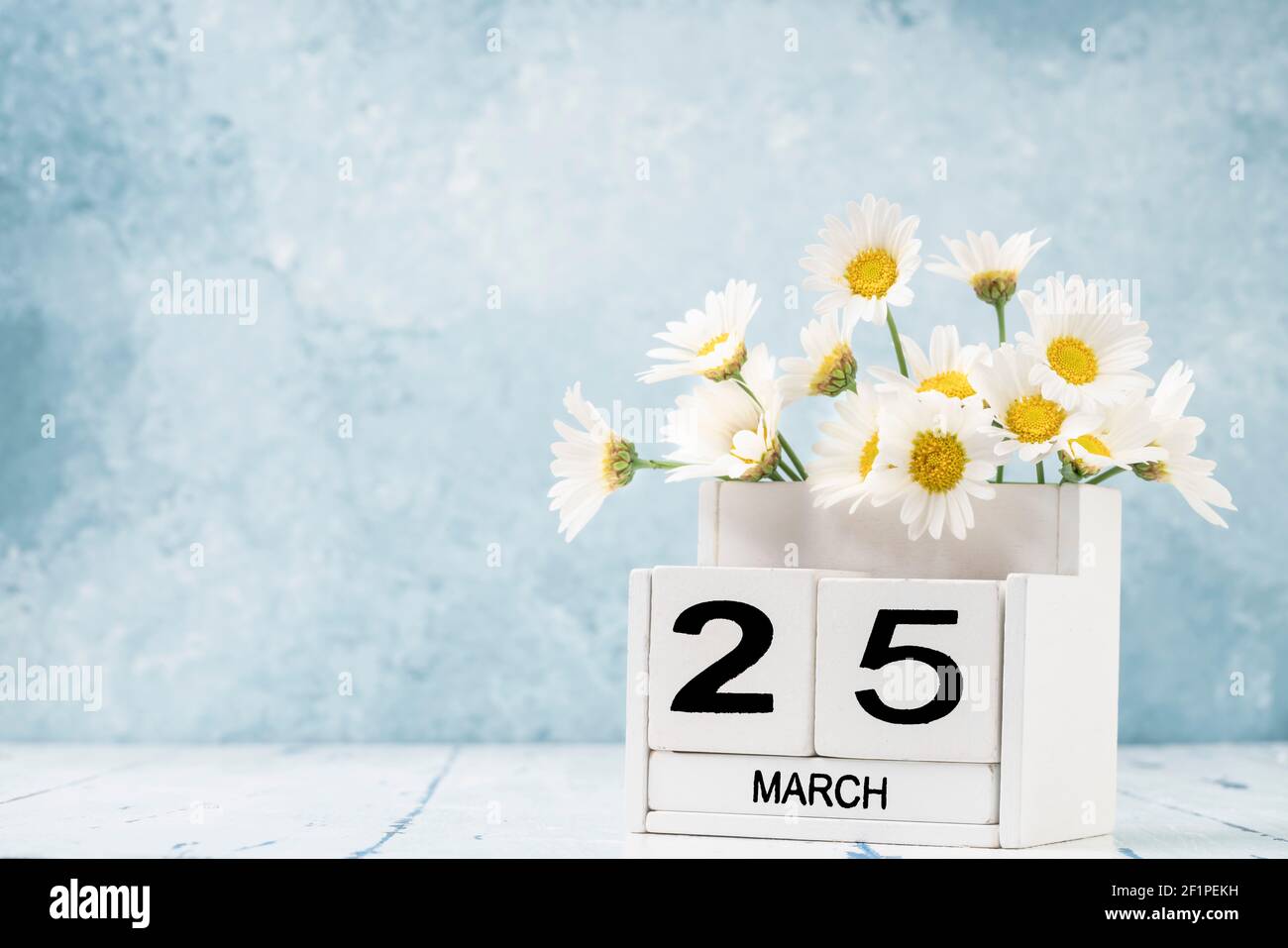 White cube calendar for march decorated with daisy flowers over blue ...