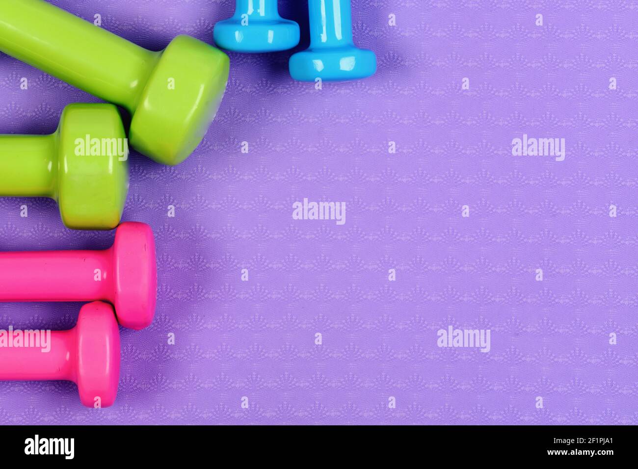 Dumbbells made of pink, green and blue plastic on purple texture ...