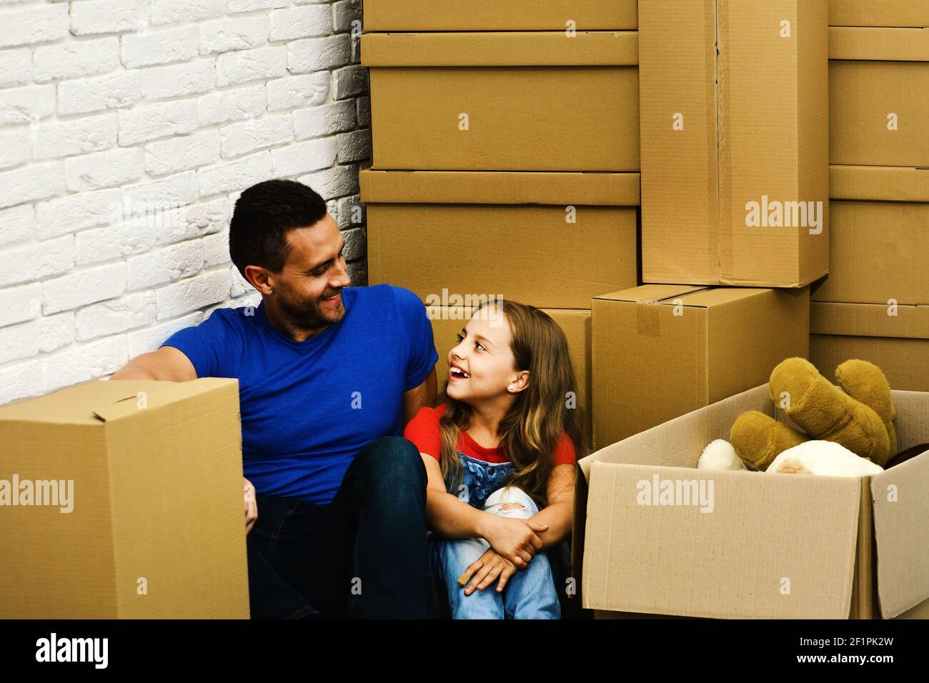 Dad and daughter sit by pile of cardboard boxes. Man and girl near box ...