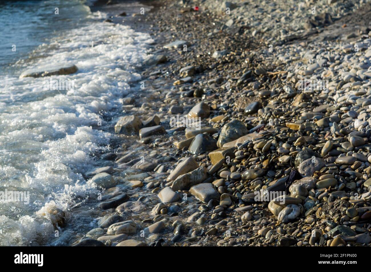 pebble stones on the sea beach on a warm summer day, the rolling waves of the blue sea with ...
