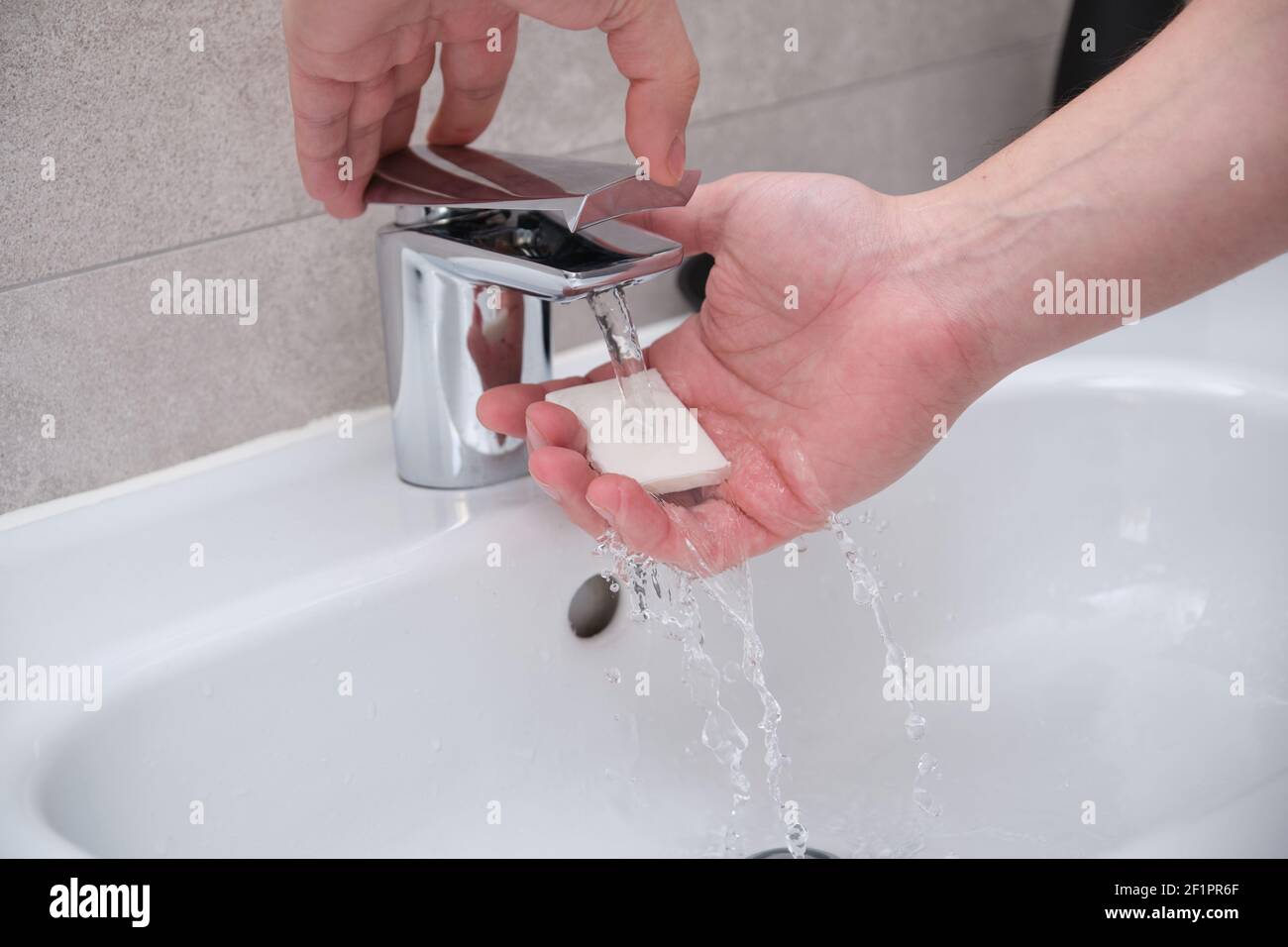 Hands holding a bar of soap and opening the tap. Washing hands process ...