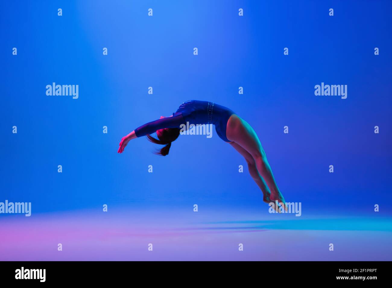 Jumping high. Young flexible girl isolated on blue studio background in ...