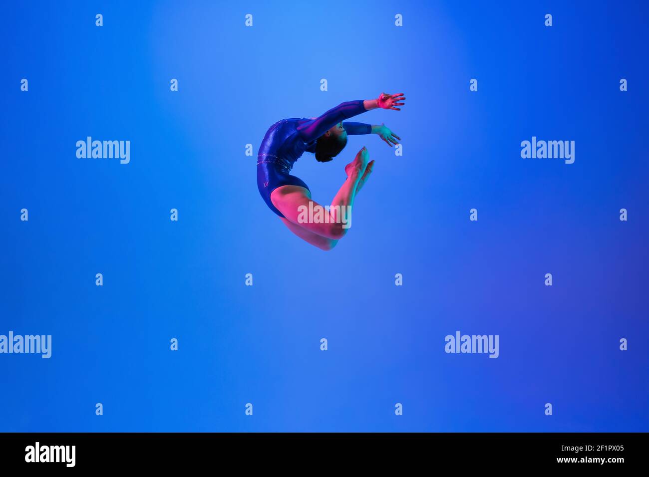 Flying high. Young flexible girl isolated on blue studio background in ...