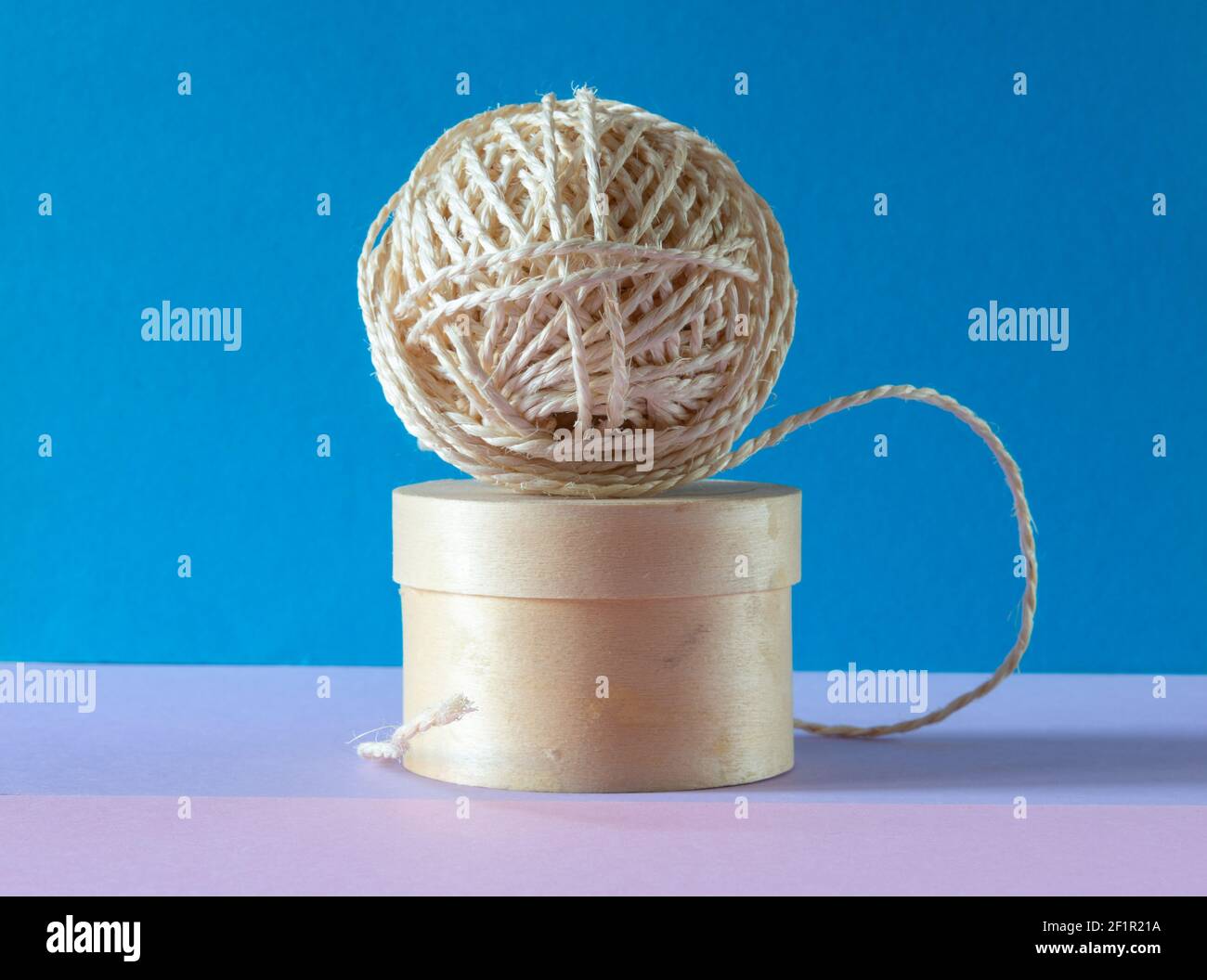 ball of string on a wooden pedestal with a blue and pink background ...