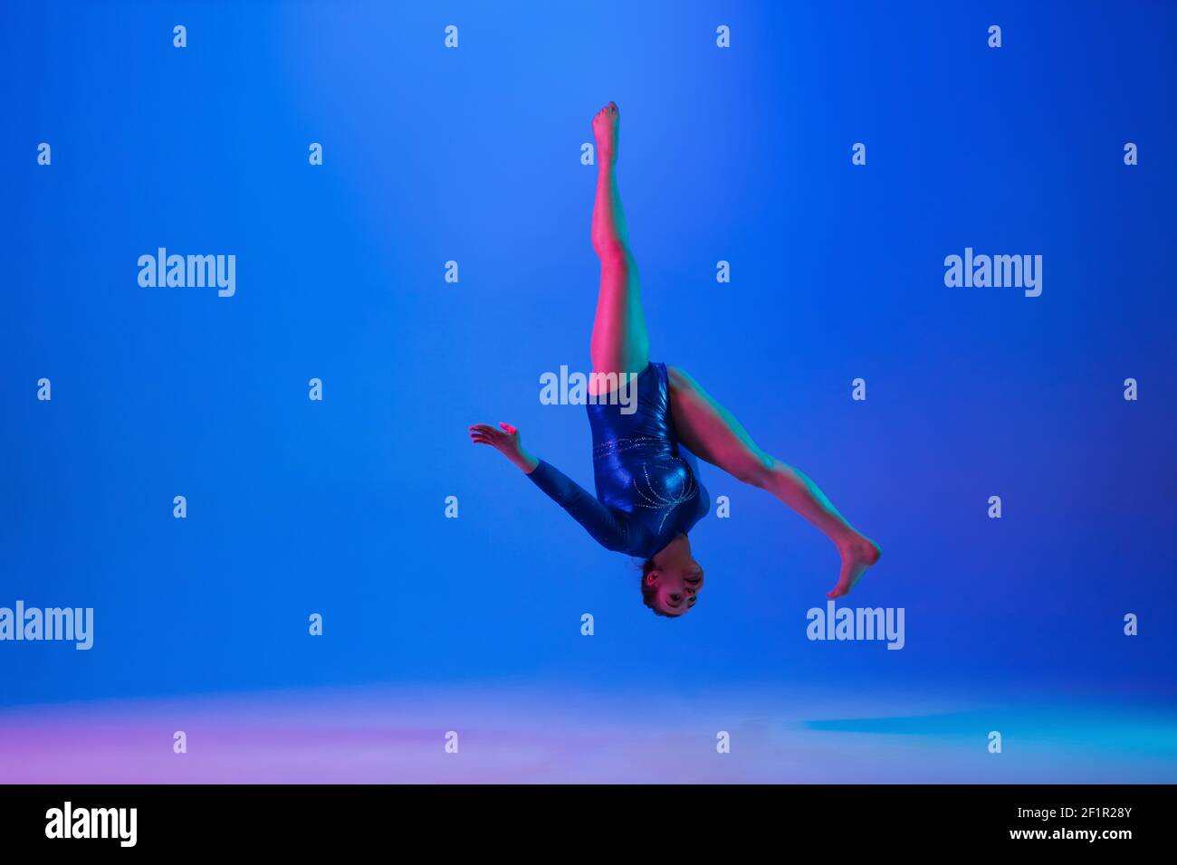 Jumping high. Young flexible girl isolated on blue studio background in ...