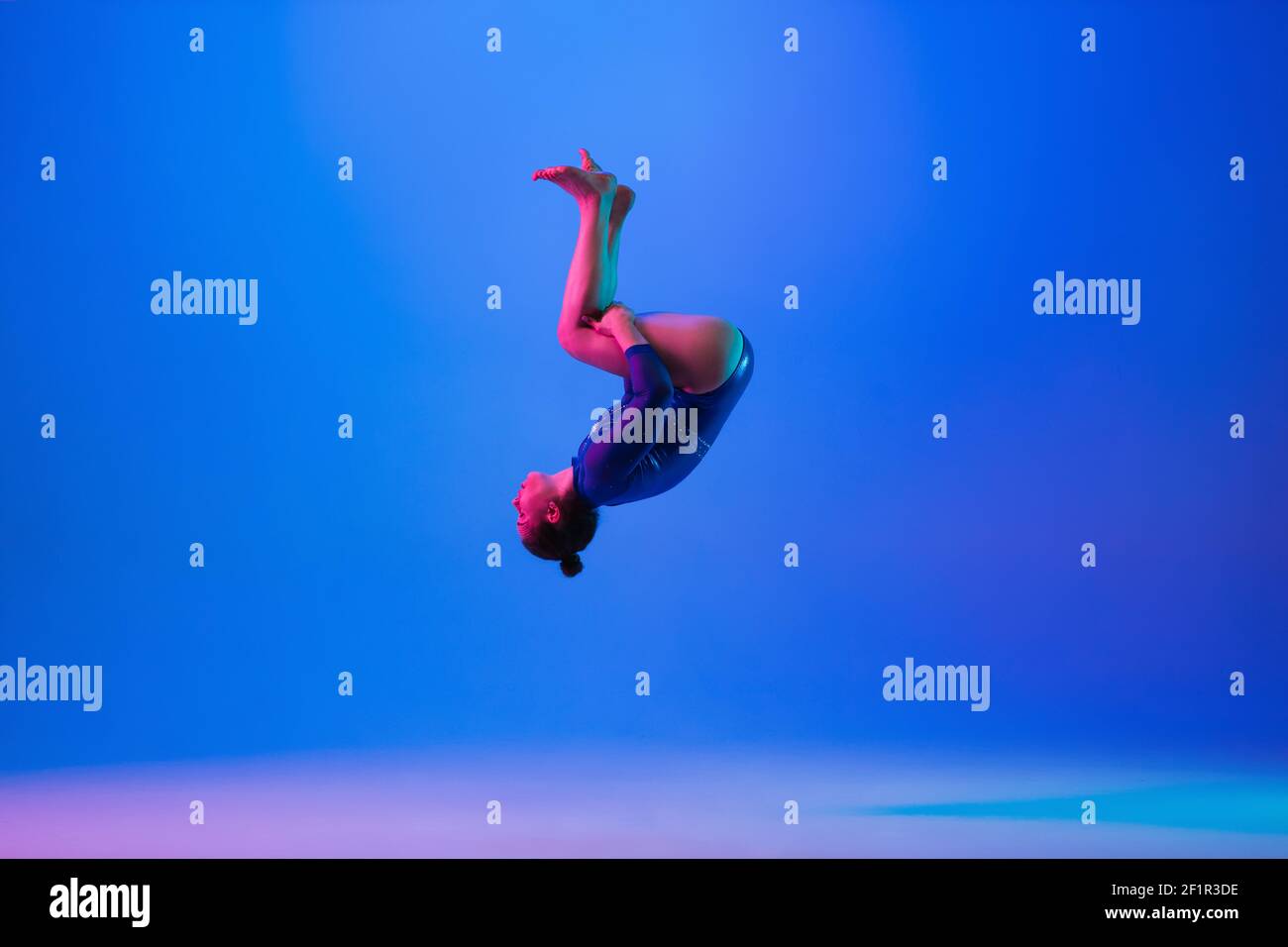Flying high. Young flexible girl isolated on blue studio background in ...