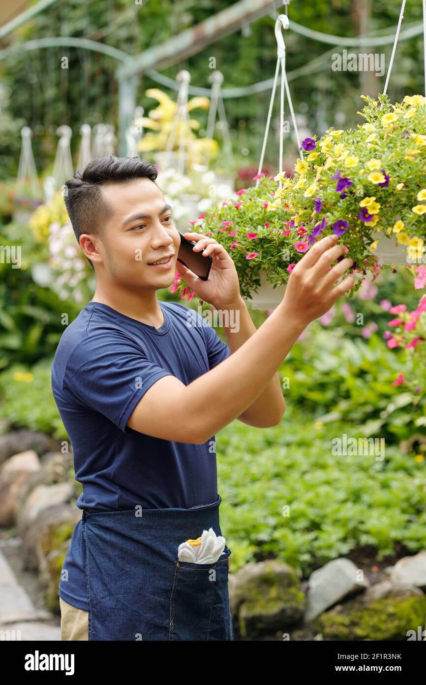 Positive young Vietnamese man talking on phone with customer and giving ...