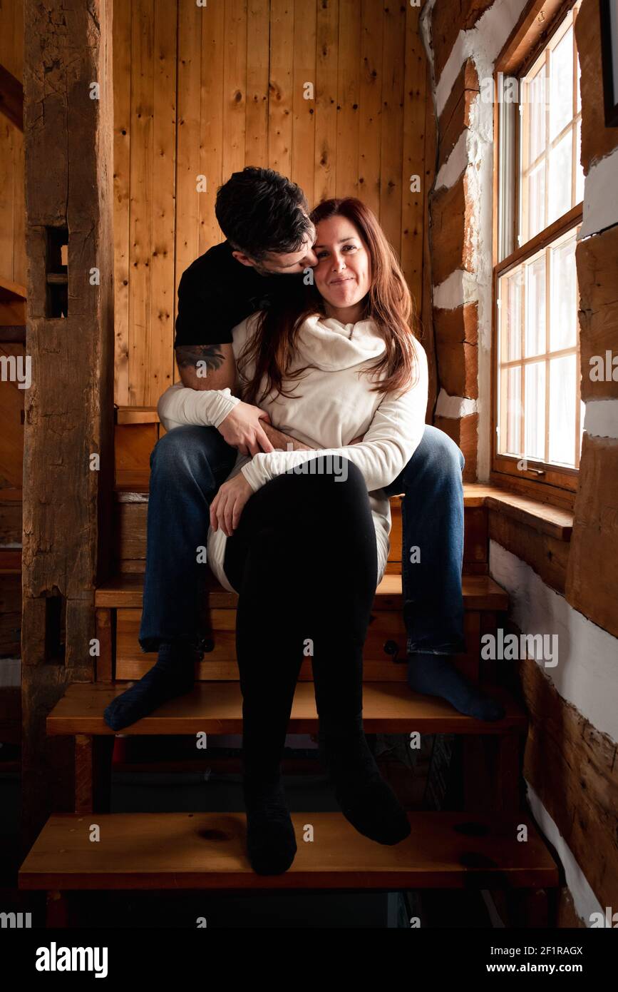 Attractive couple sitting on stairs together inside rustic log cabin ...