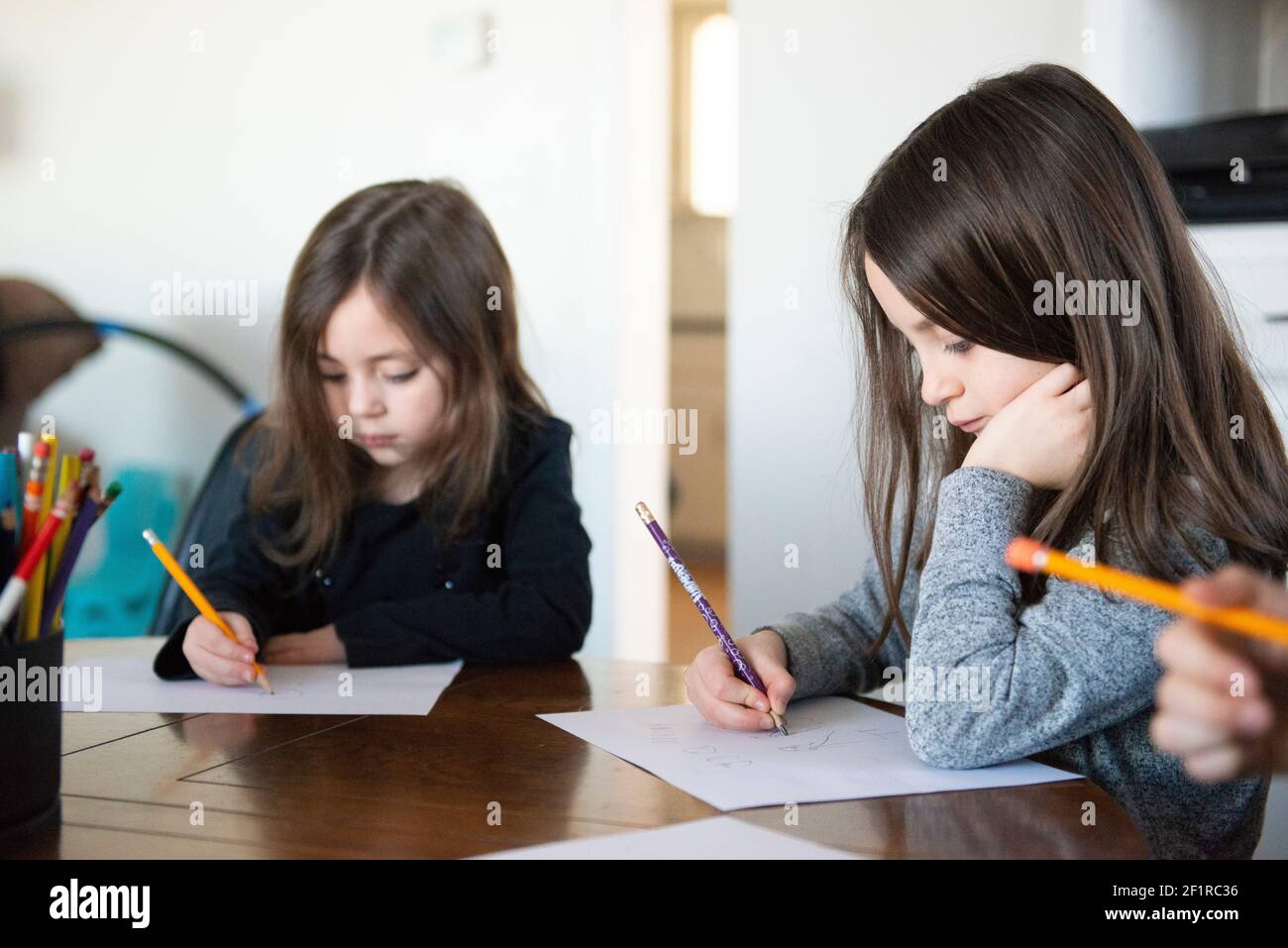 Two young girls sitting at a table doing schoolwork Stock Photo - Alamy
