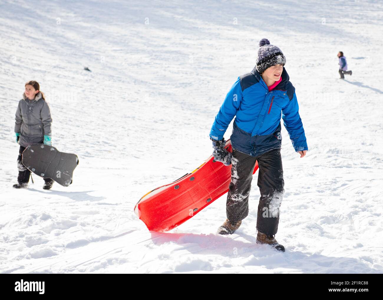 Boy walking up a sledding hill with orange sled Stock Photo - Alamy