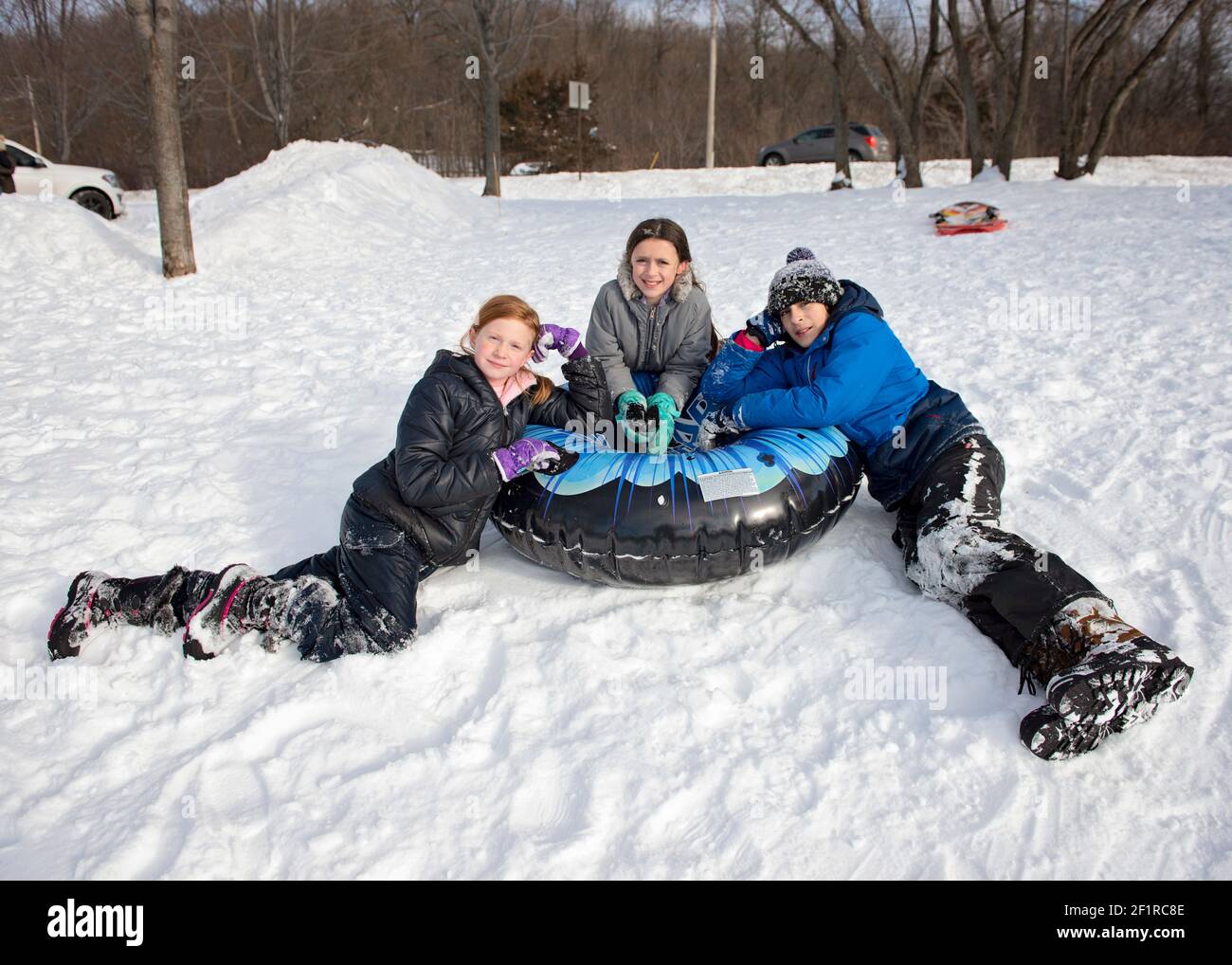 Tree kids around a snow tube on a sledding hill in winter Stock Photo ...