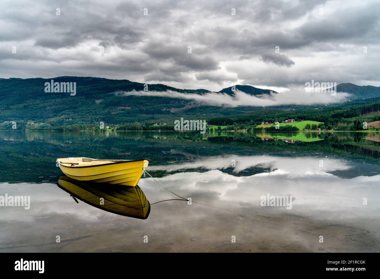A single yellow row boat floats in a perfectly calm lake which creates ...